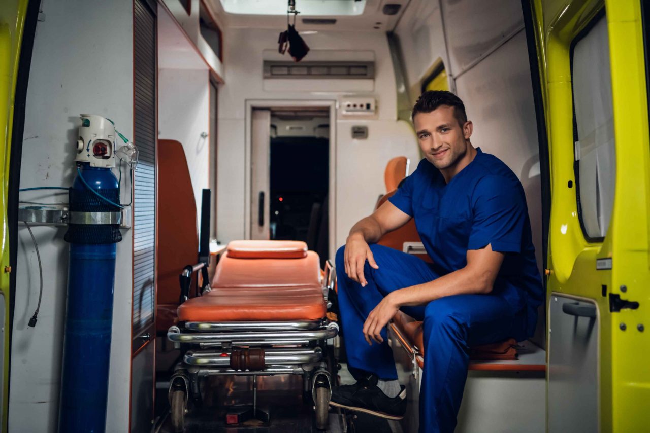 smiling-paramedic-blue-uniform-sitting-back-ambulance-car | calmo.co.id